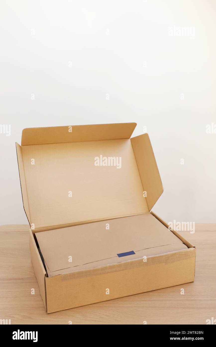 Open cardboard box with item wrapped in kraft paper on wooden table ...