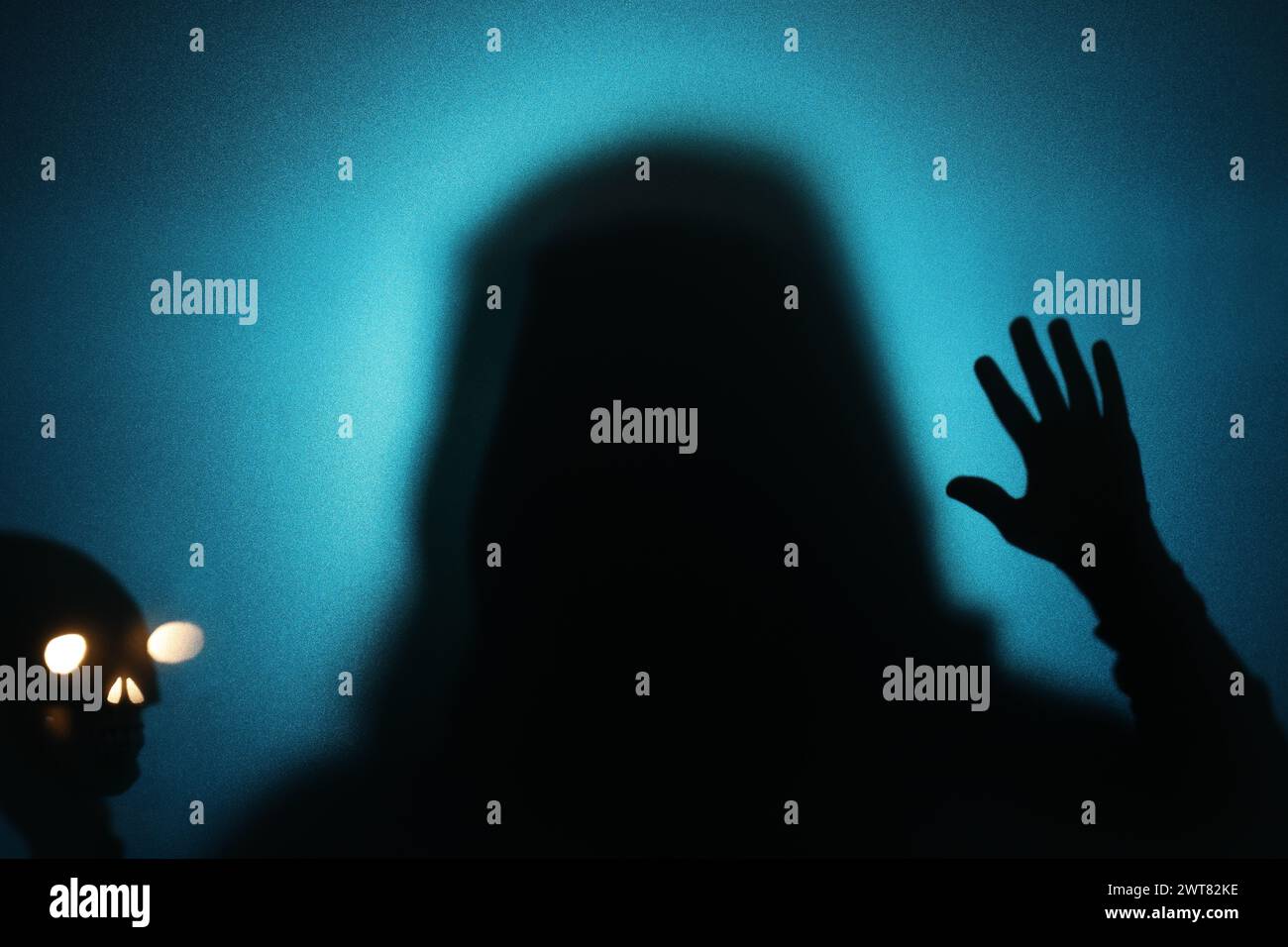 Silhouette of ghost and skull behind glass against blue background ...