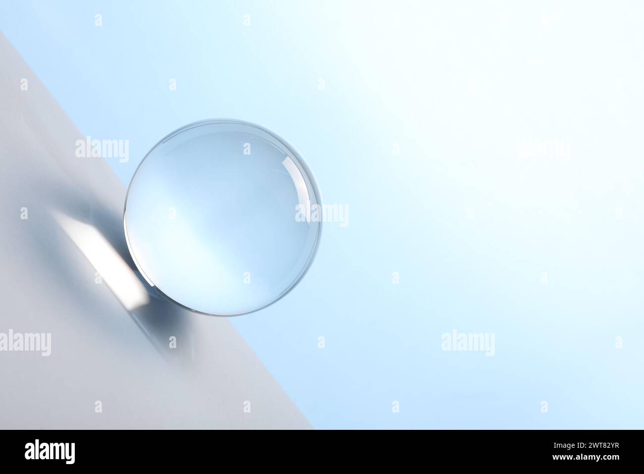 Transparent glass ball on table against light blue background. Space ...