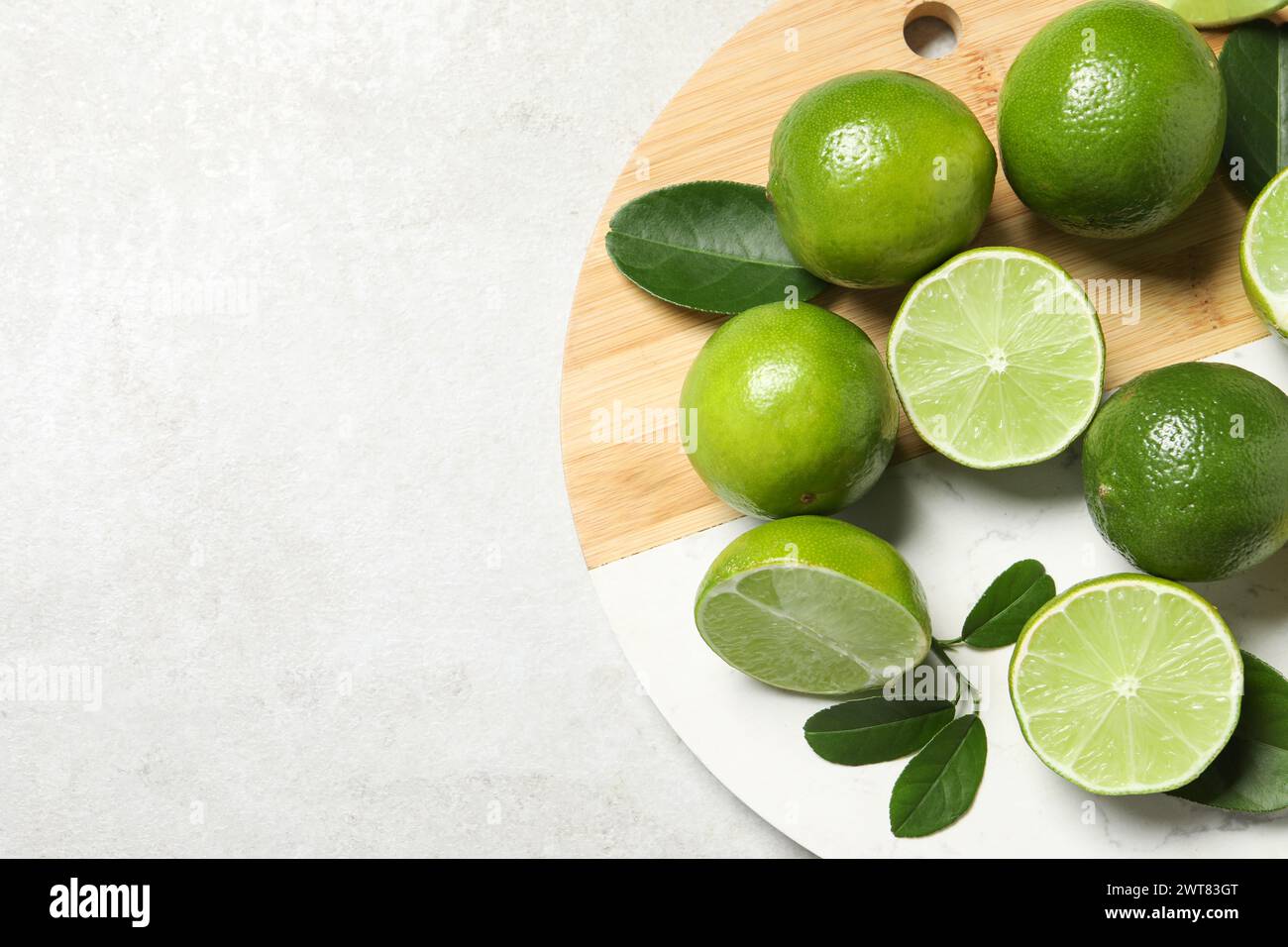Fresh ripe limes and leaves on light table, top view. Space for text ...