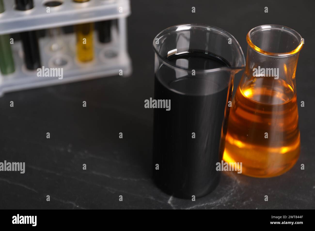 Beaker and flask with different types of oil on grey textured table ...