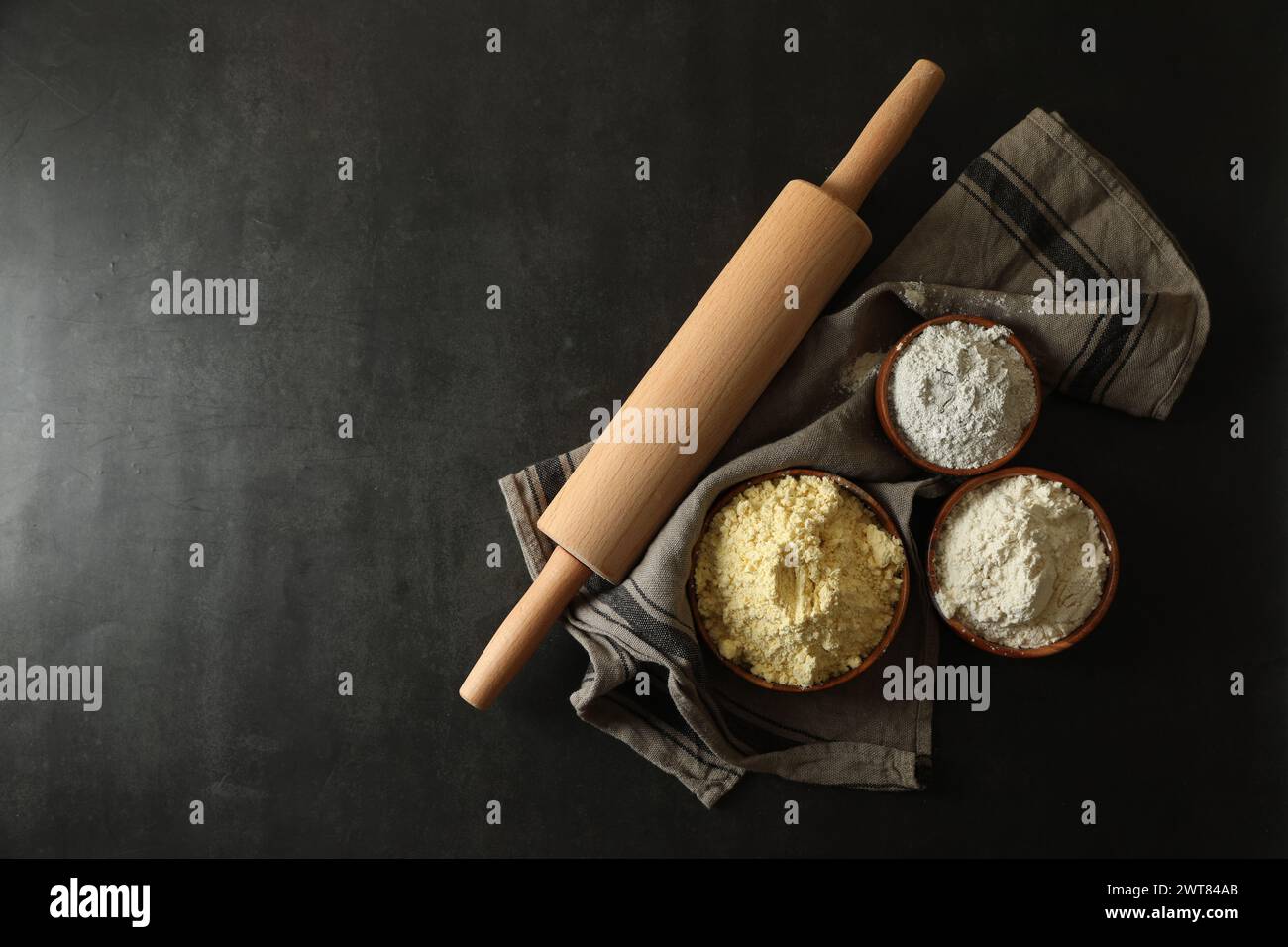 Rolling pin and different types of flour on black table, top view ...