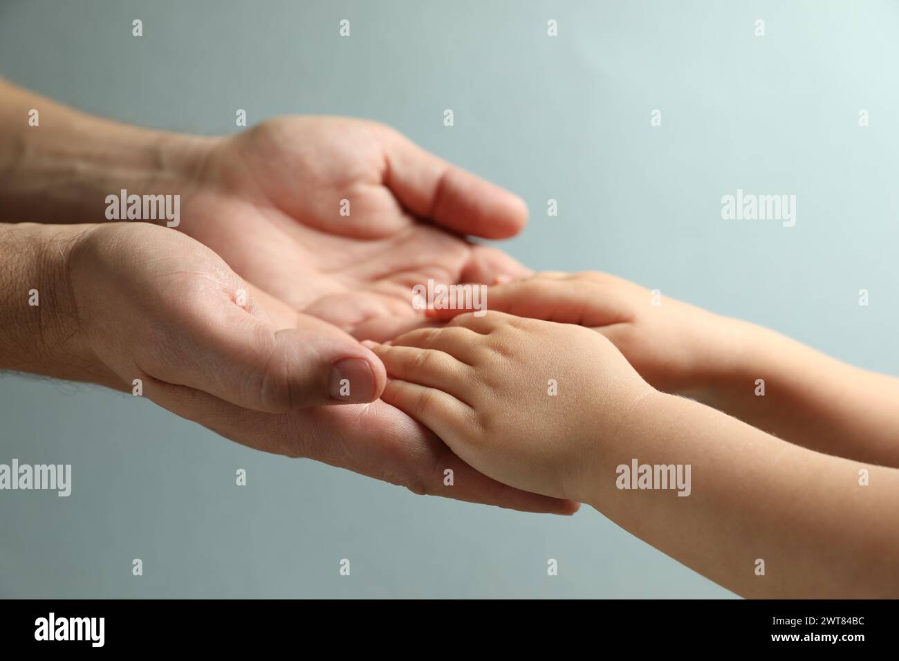 Father and child holding hands on light blue background, closeup Stock ...