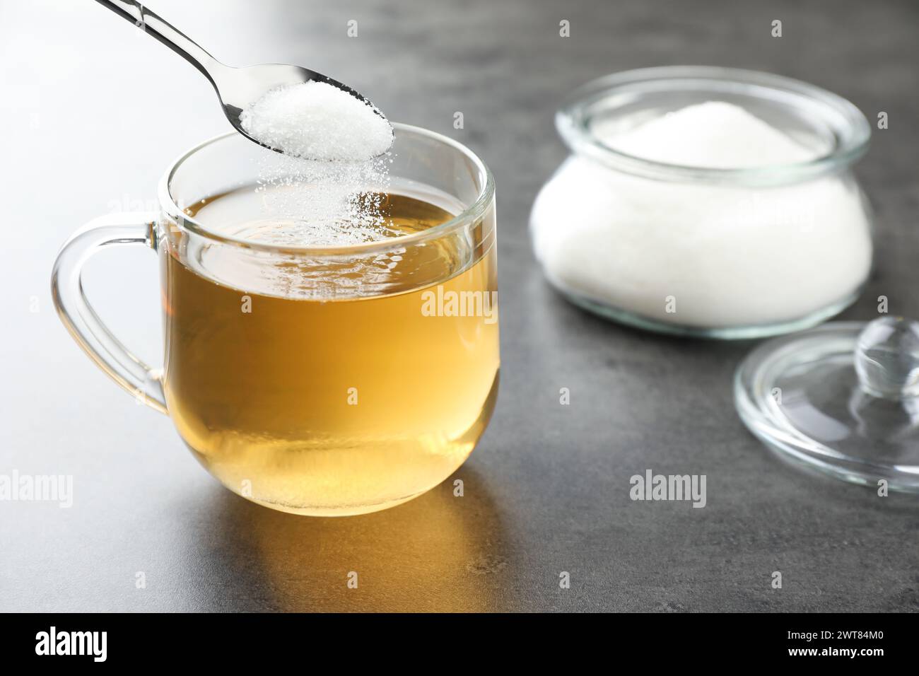Adding sugar into aromatic tea at grey table, closeup Stock Photo - Alamy