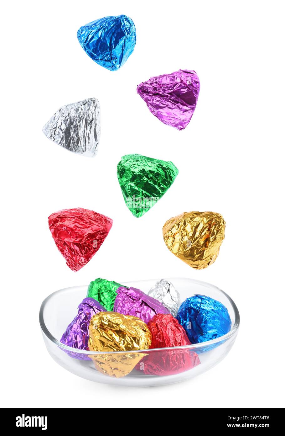 Tasty candies in bright wrappers falling into glass bowl on white ...