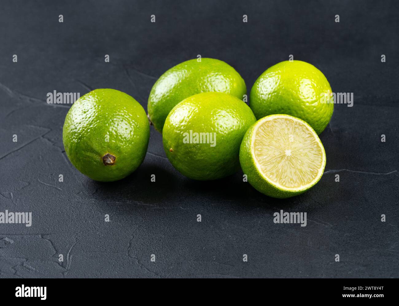 Several fresh lime fruits with a juicy half on a dark background Stock ...