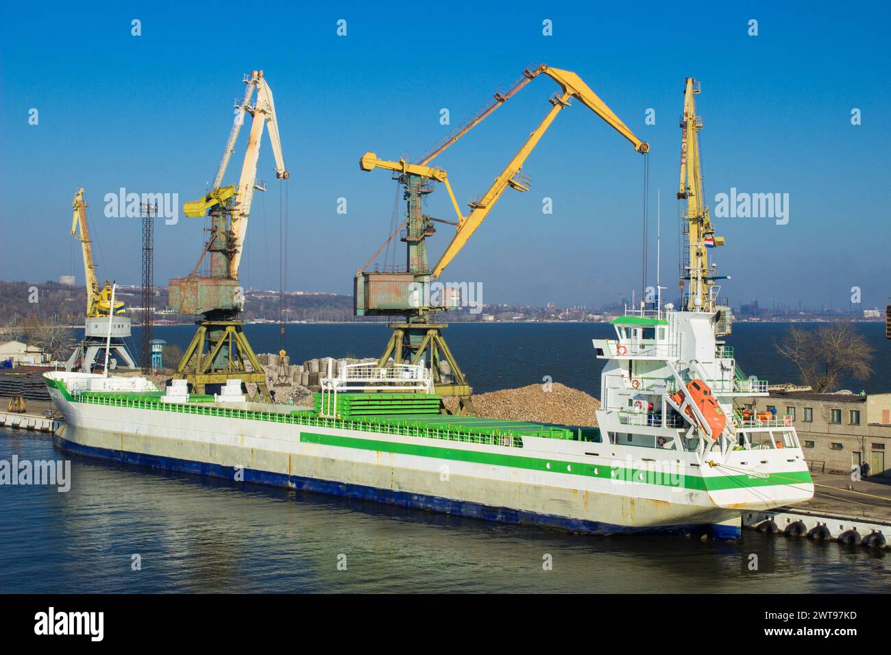 Cargo ship docked at international port, cranes loading containers under clear sky. Maritime ...