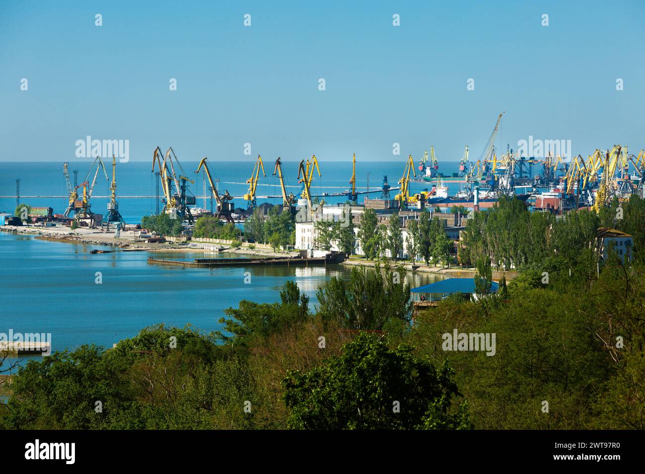 Coastal industrial port, cargo cranes dominate skyline. Ships docked at ...