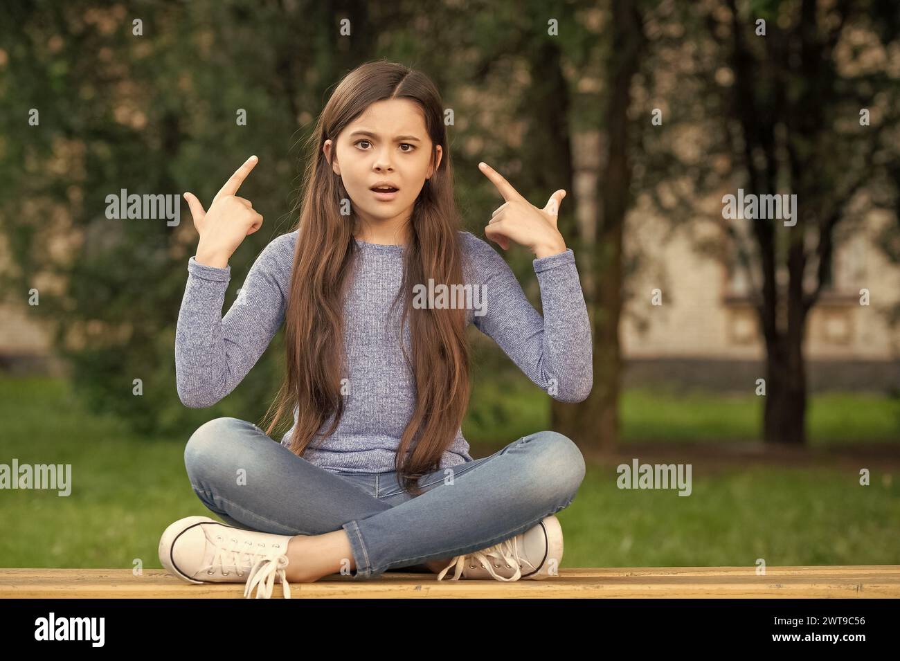 Pointing fingers. Confused teen girl pointing at head sitting leg ...