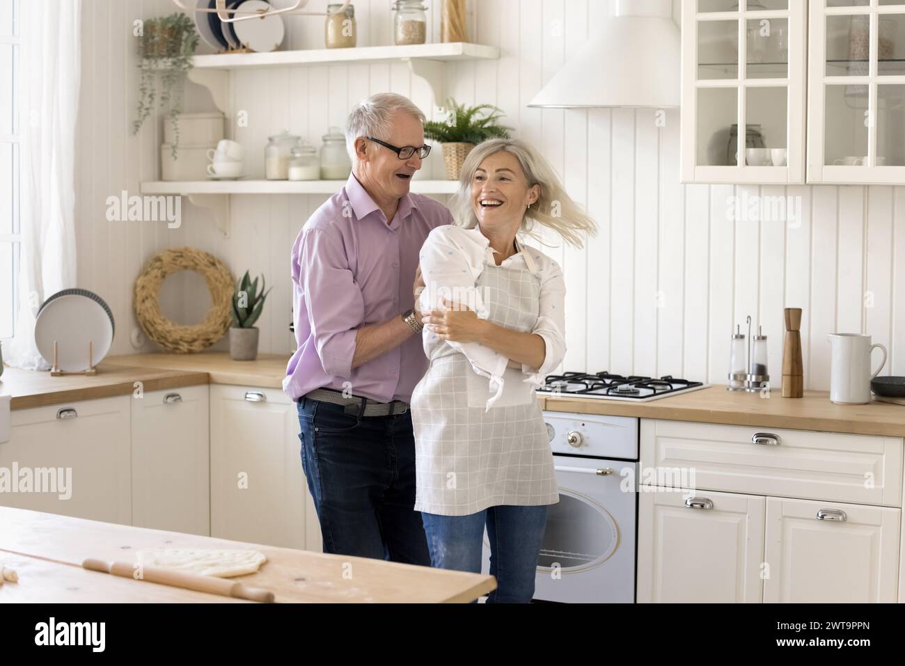 Active, energetic mature couple dancing in kitchen while cooking ...