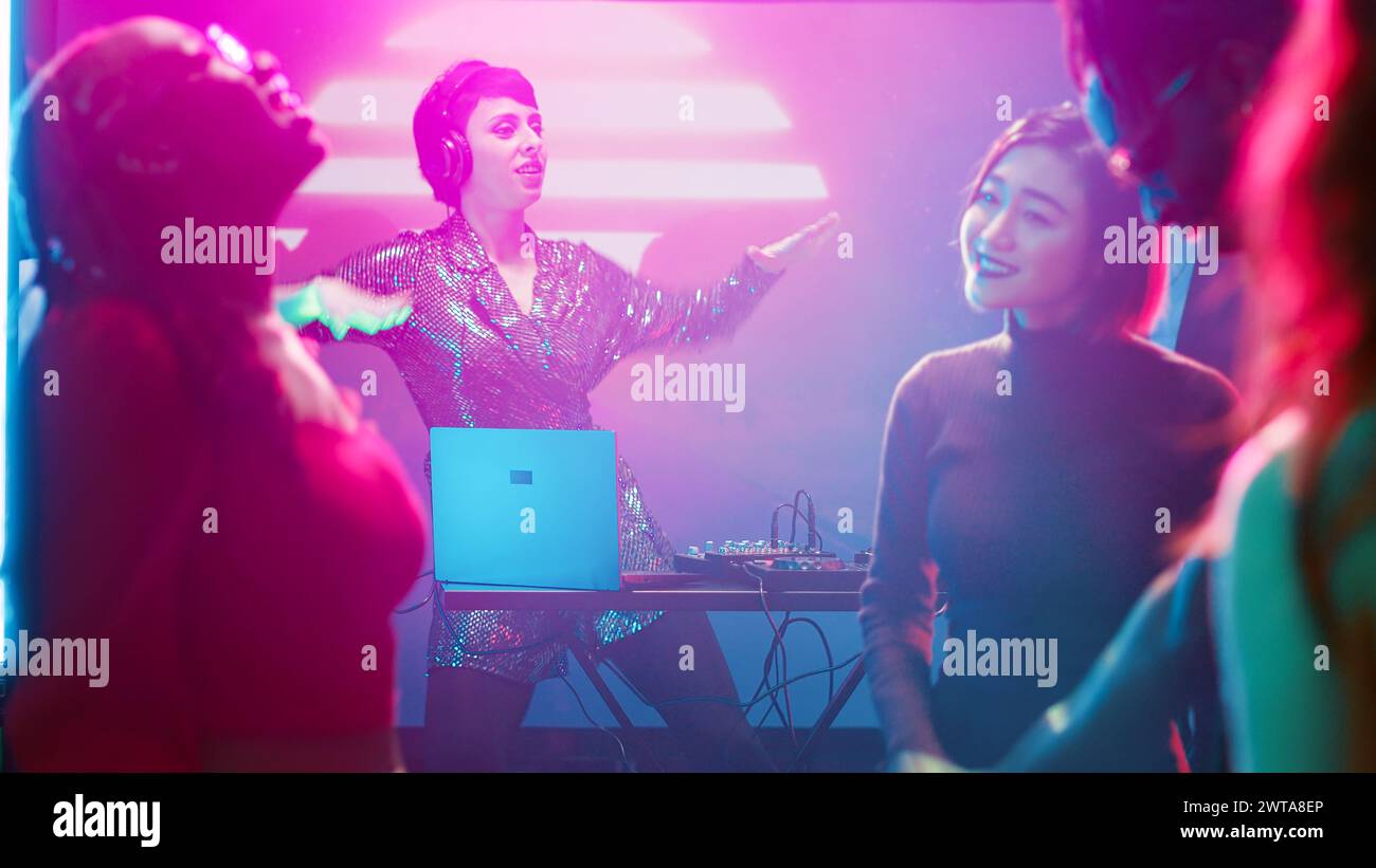 Funky female DJ mixing sounds on stage at club, dancing with group of ...
