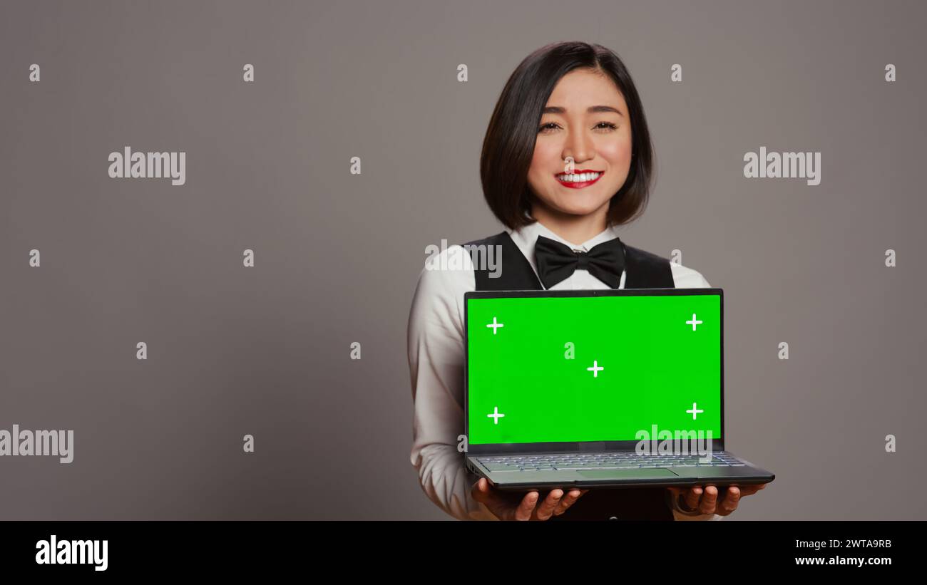 Asian hotel concierge holding pc with greenscreen on camera, presenting ...