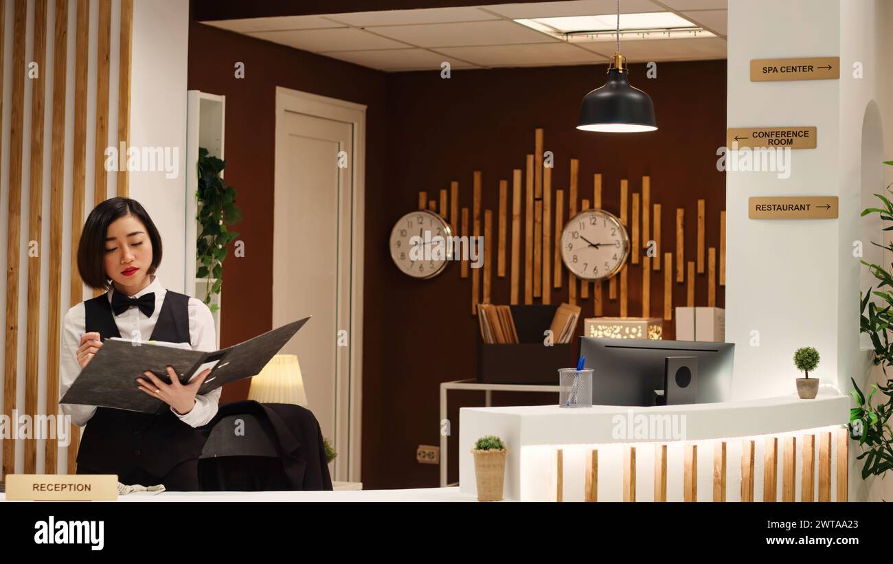Professional asian receptionist cross referencing tourists booking ...