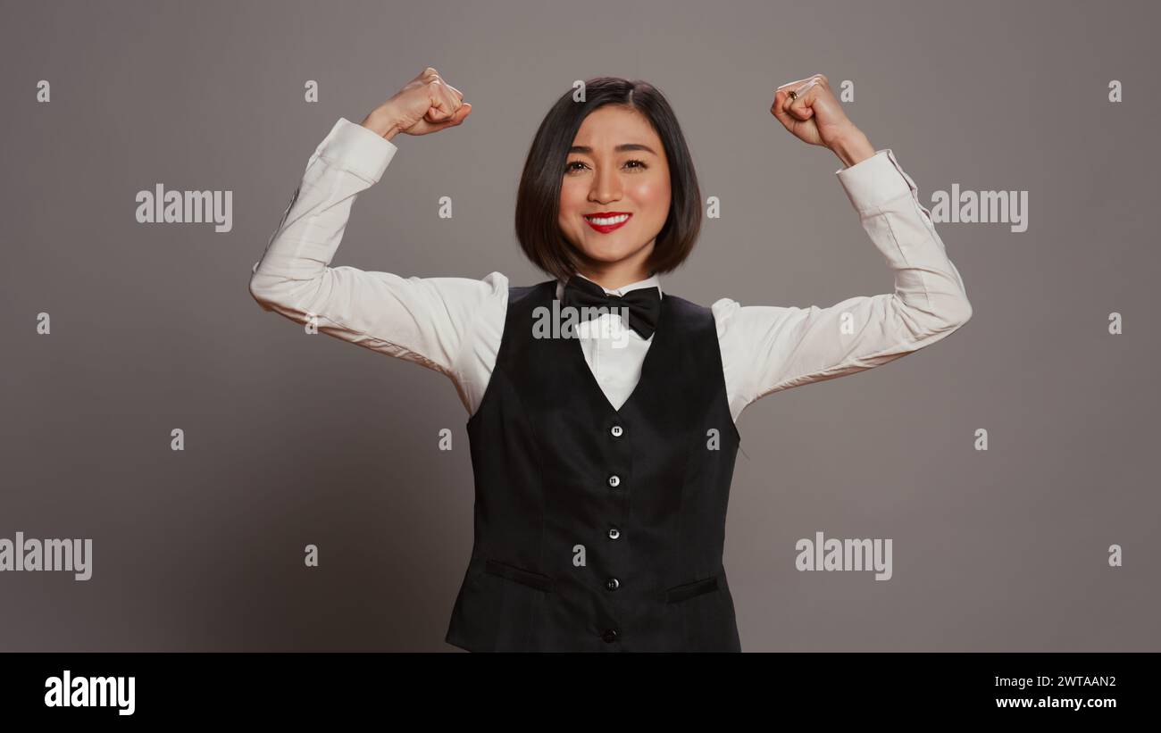 Asian hotel concierge flexing arms muscles in grey studio, showing off ...