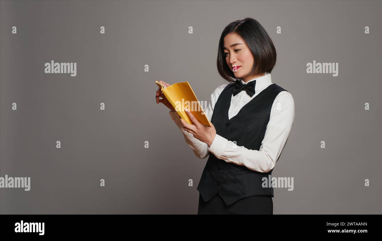 Asian receptionist reading a literature book over grey background ...