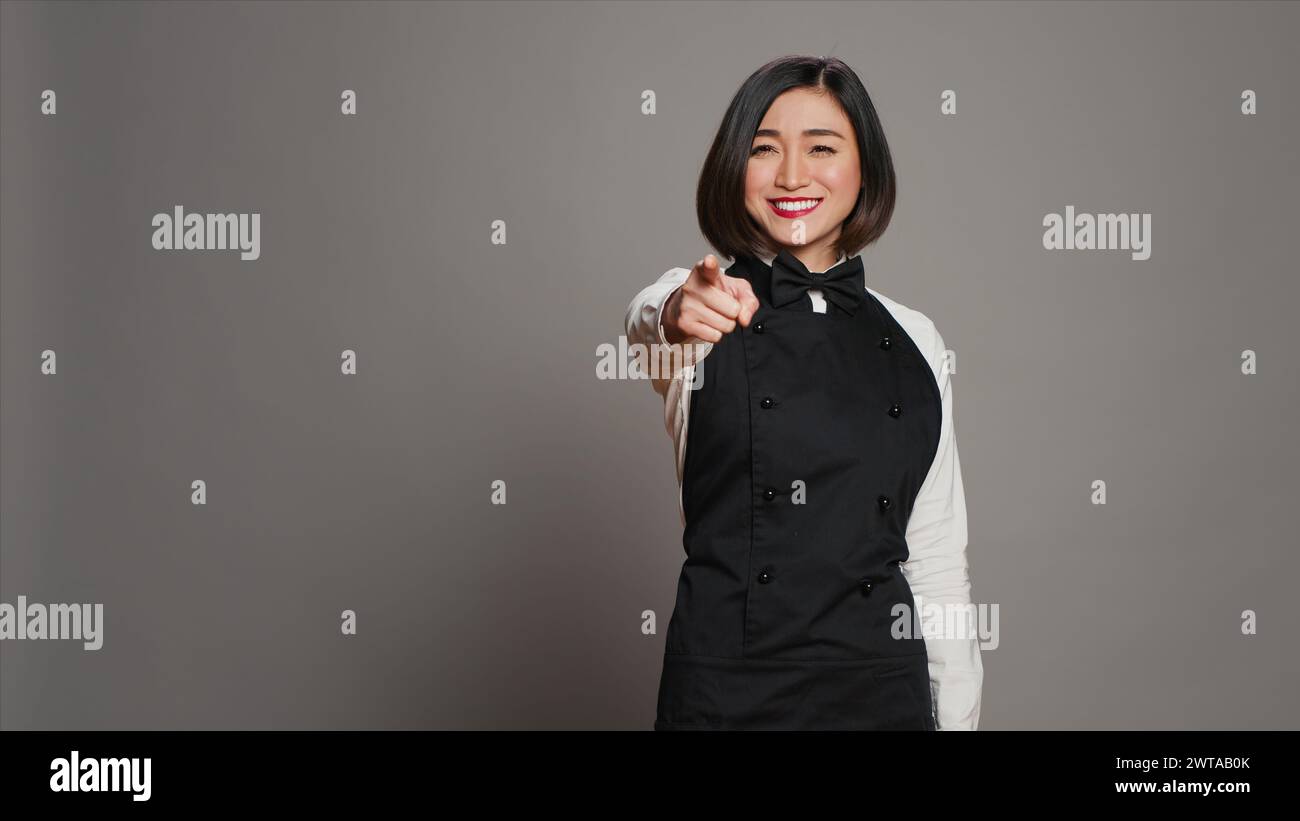 Asian waitress pointing at camera to choose you over grey background ...