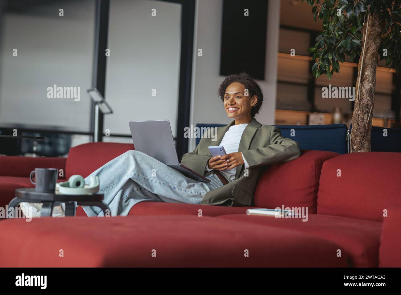 Woman on red couch in nice modern coworking office, using laptop and ...