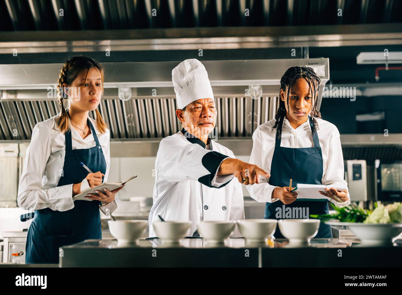 Professional Asian senior chef guides diverse students in a restaurant ...