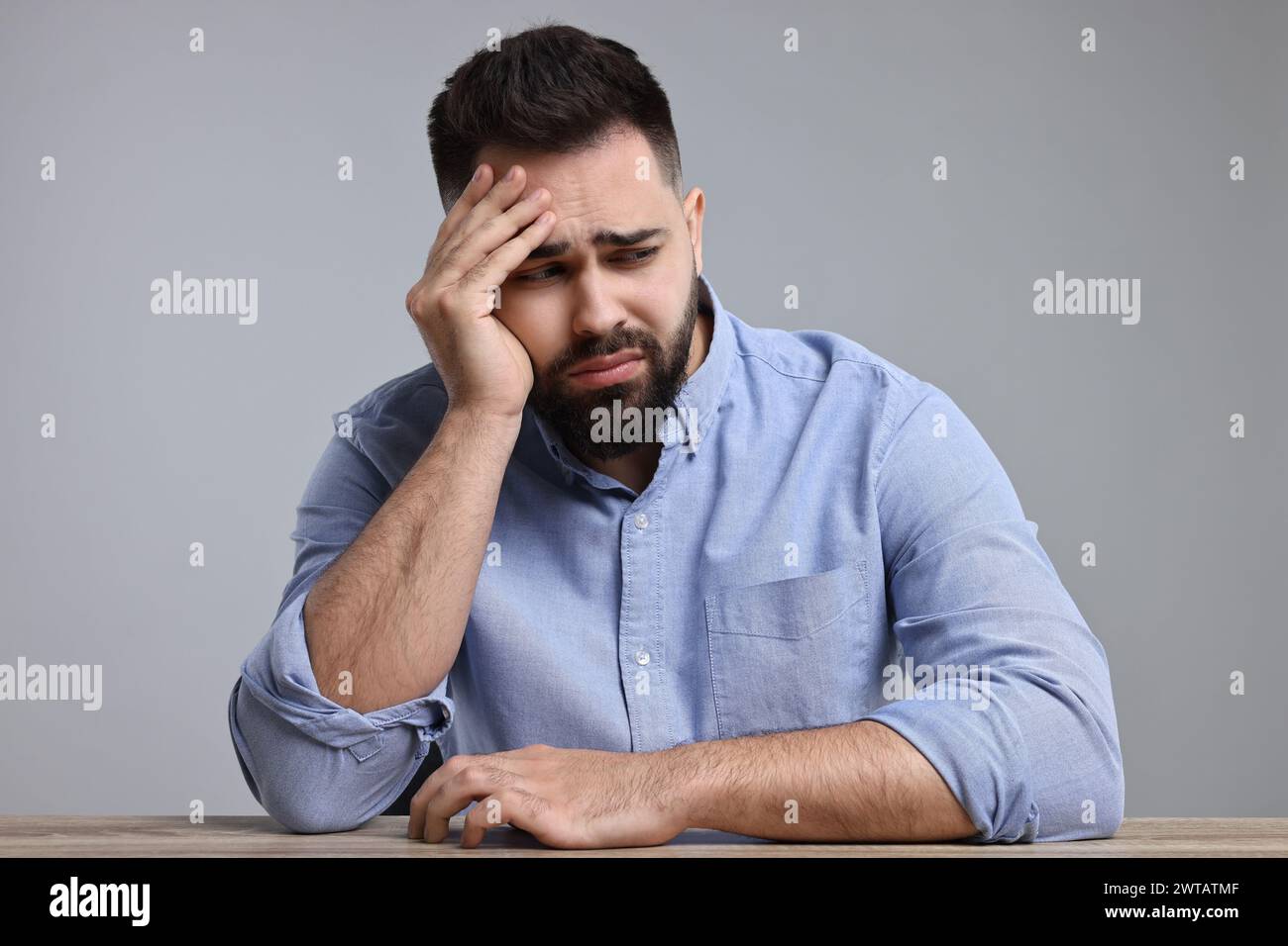 Portrait of sad man at wooden table on light grey background Stock ...