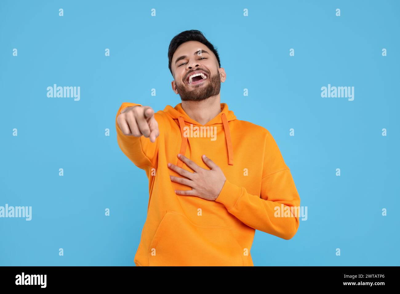 Handsome young man laughing while pointing at something on light blue ...