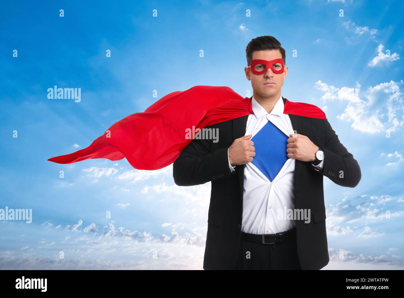Confident man wearing superhero cape and mask taking suit off against ...