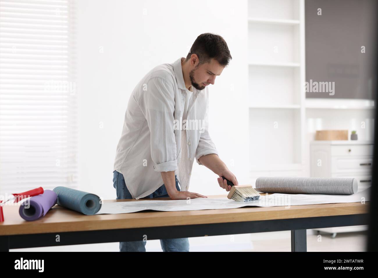 Man applying glue onto wallpaper sheet at wooden table indoors Stock ...