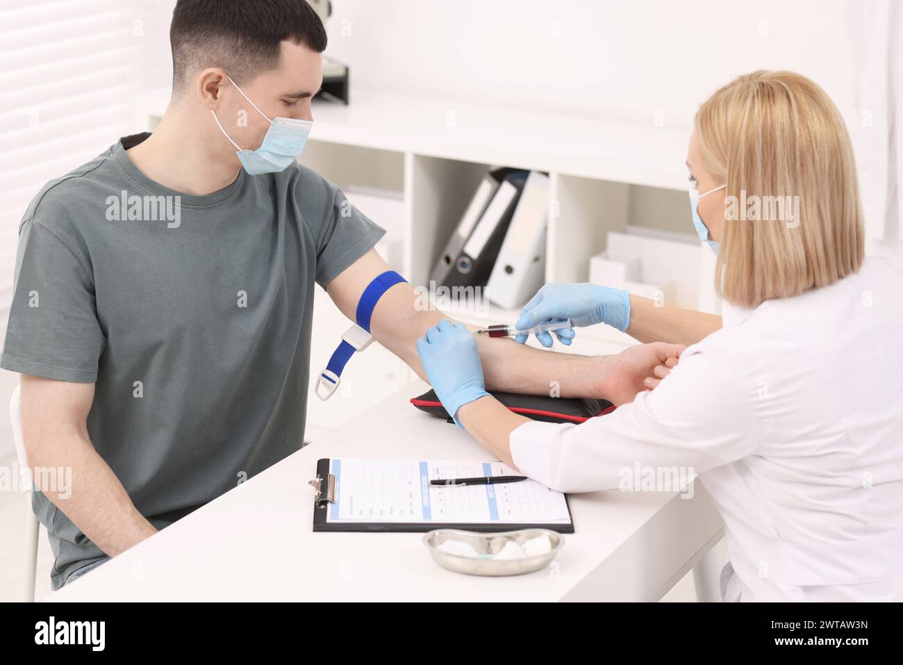 Doctor taking blood sample from patient with syringe at white table in ...