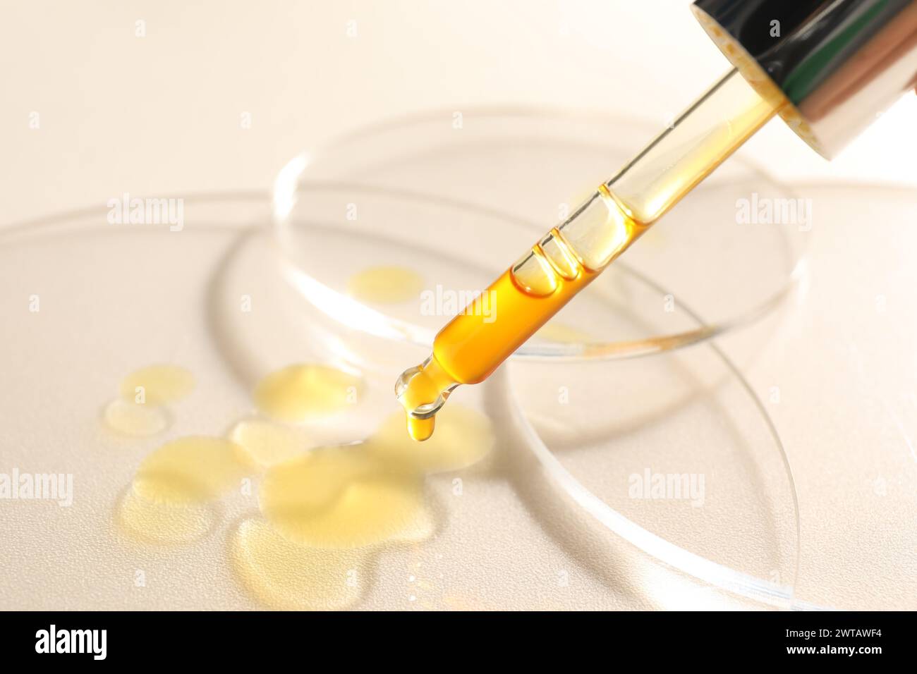 Dripping moisturizing serum from pipette on beige background, closeup ...