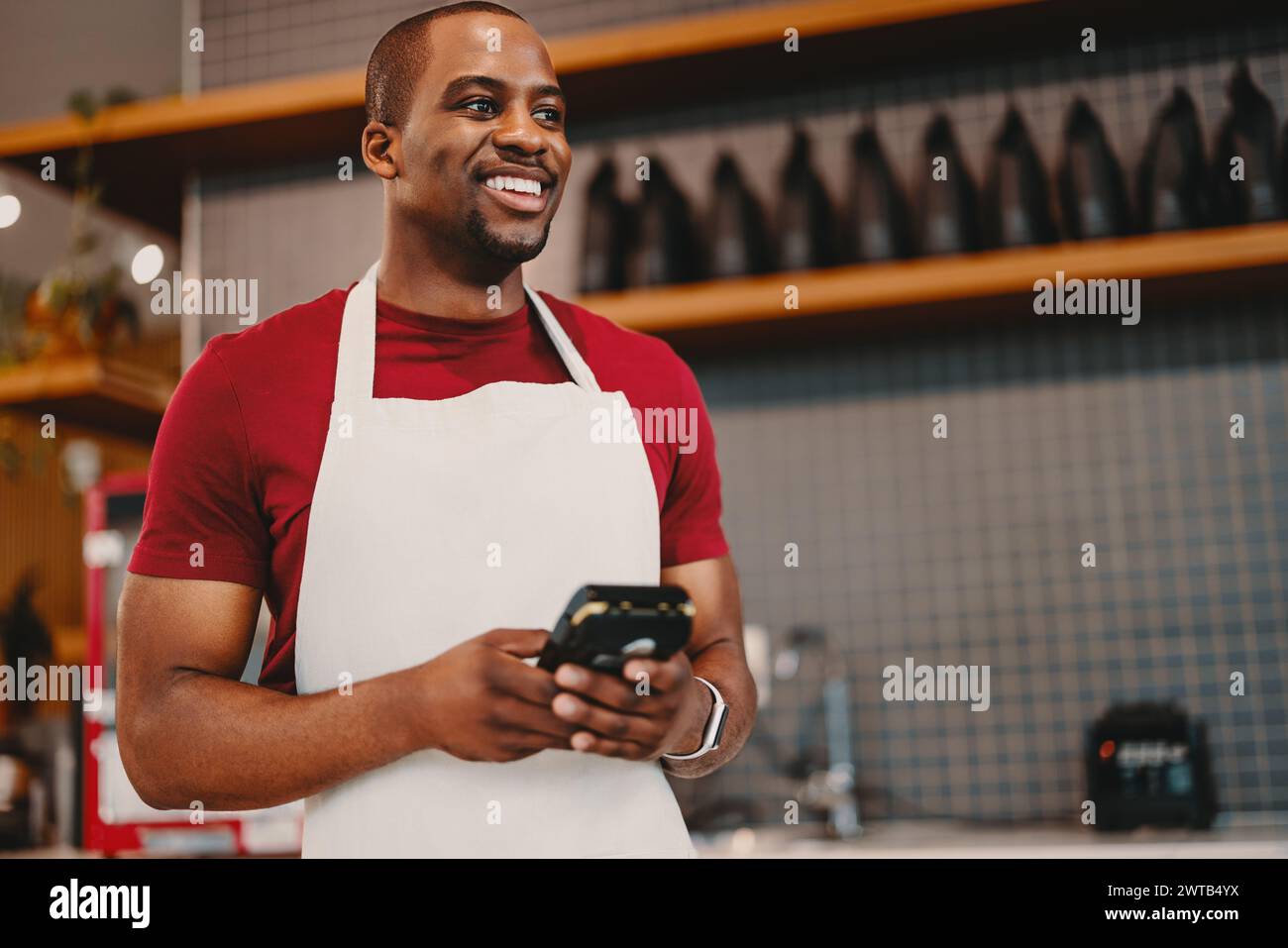 Cheerful entrepreneur holding a pos machine in a cafe, wearing a white ...