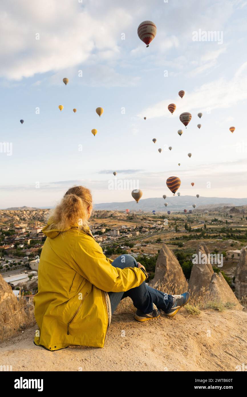 Blonde woman watching balloons flying over Cappadocia fairy chimney ...