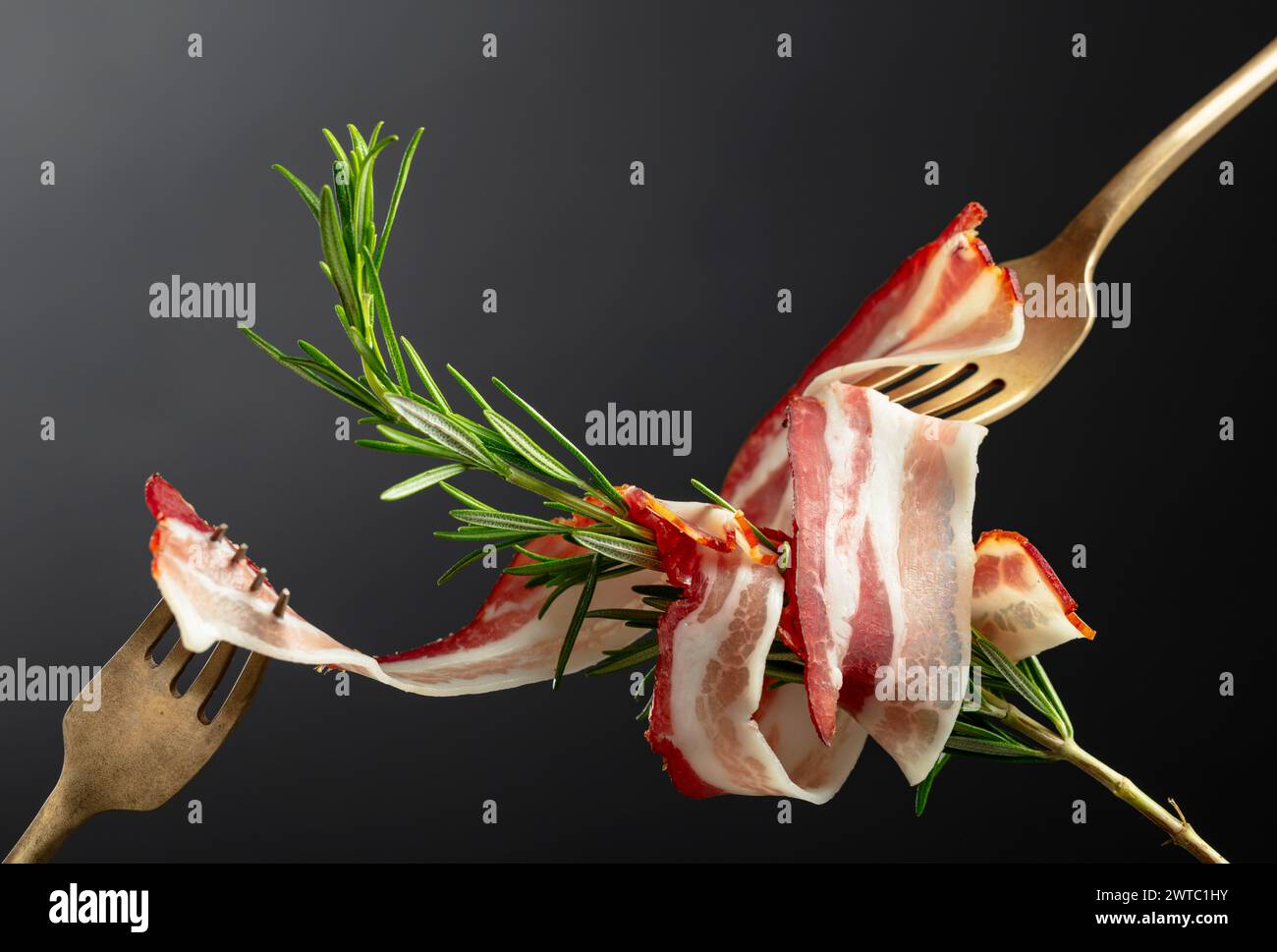 Dry-cured pork belly bacon with rosemary on a black background. Sliced ...