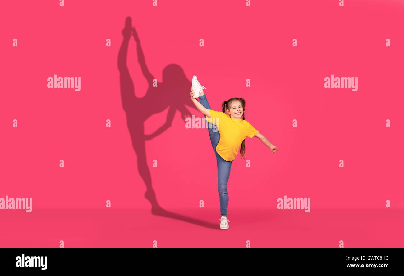 A joyful young girl in a yellow shirt and jeans performs a high leg ...