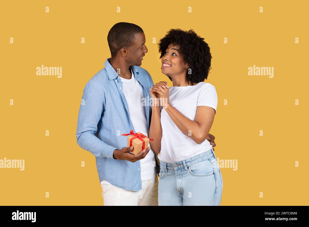 Affectionate young man gifting a small, charming box with a red bow to ...