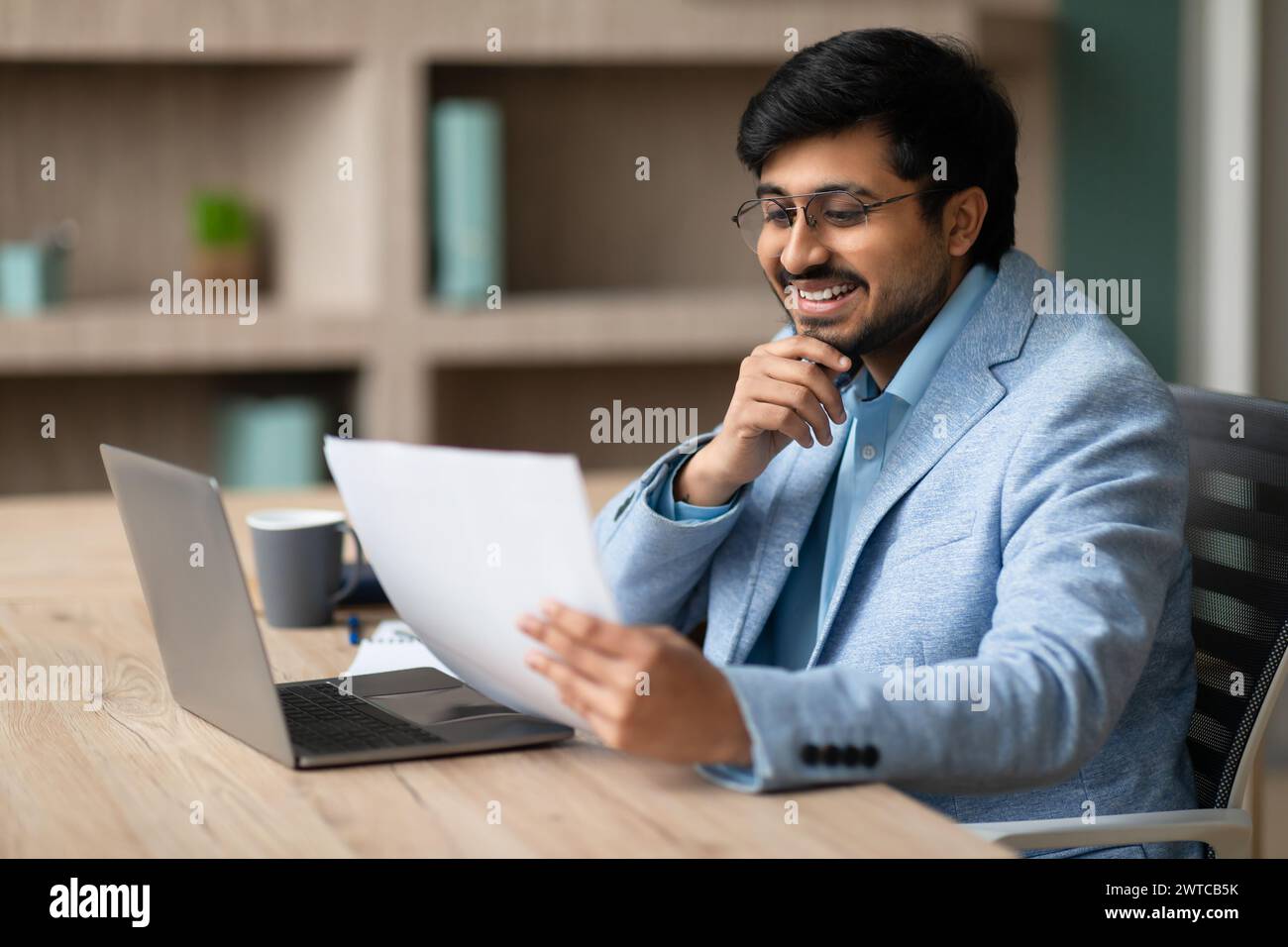 Contented Indian businessman looks through papers engrossed in work ...