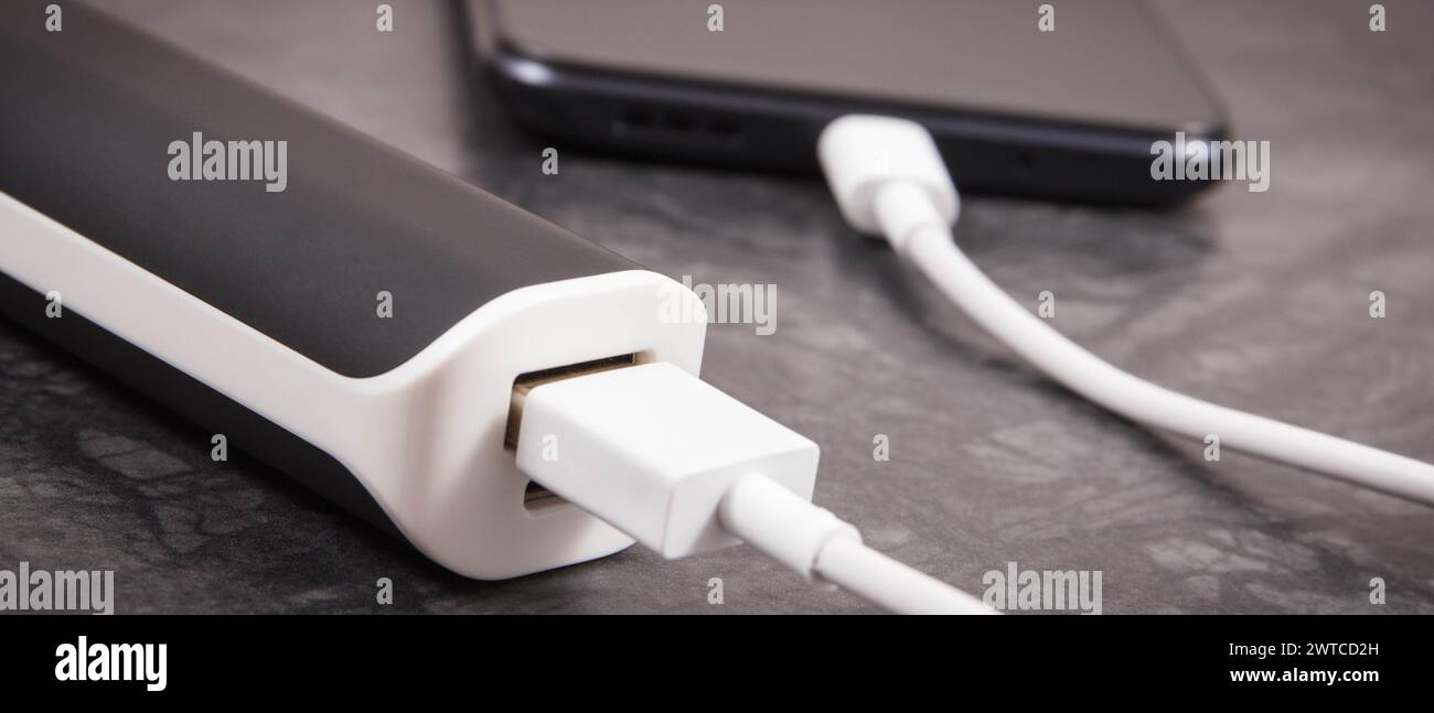 Black smartphone with connected white plug of external powerbank ...