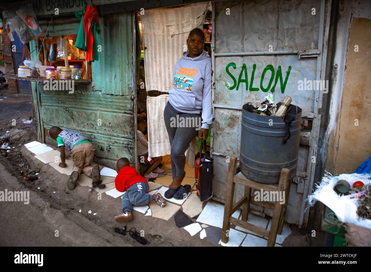 A lady is posed outside a salon in Kibera Slum watching over her kids ...