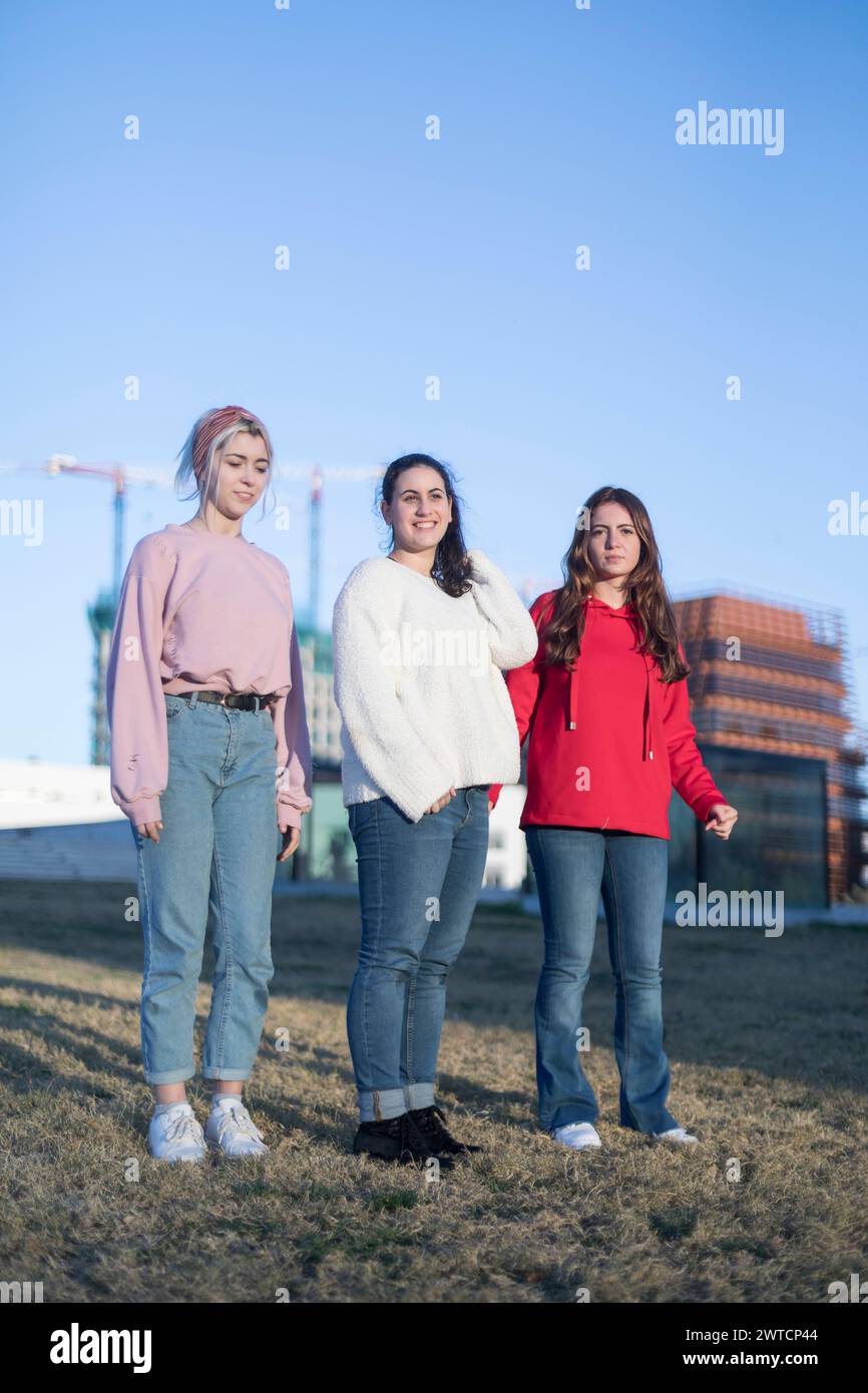 Three female friends stand in a field, posing confidently. The urban ...