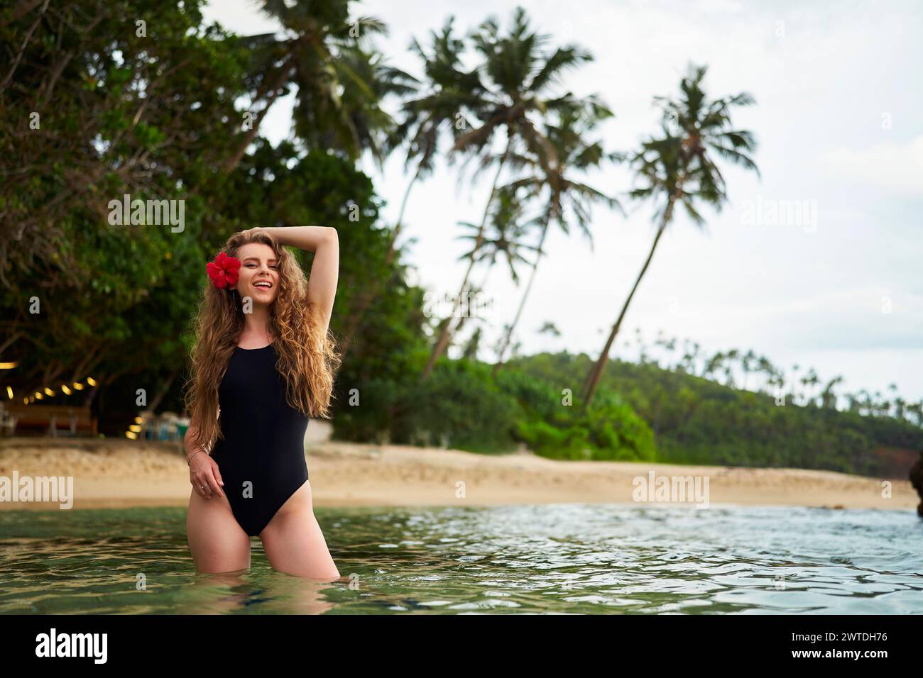 Woman in swimsuit enjoys sea swim. Female with floral hair accessory wades in tropical water ...