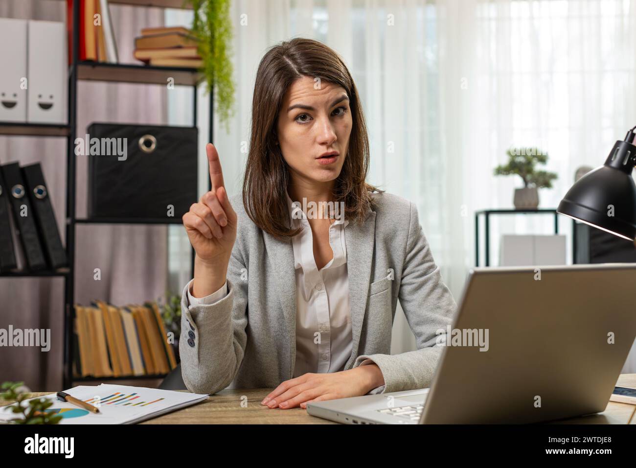 Young businesswoman working on laptop computer shakes finger and saying ...
