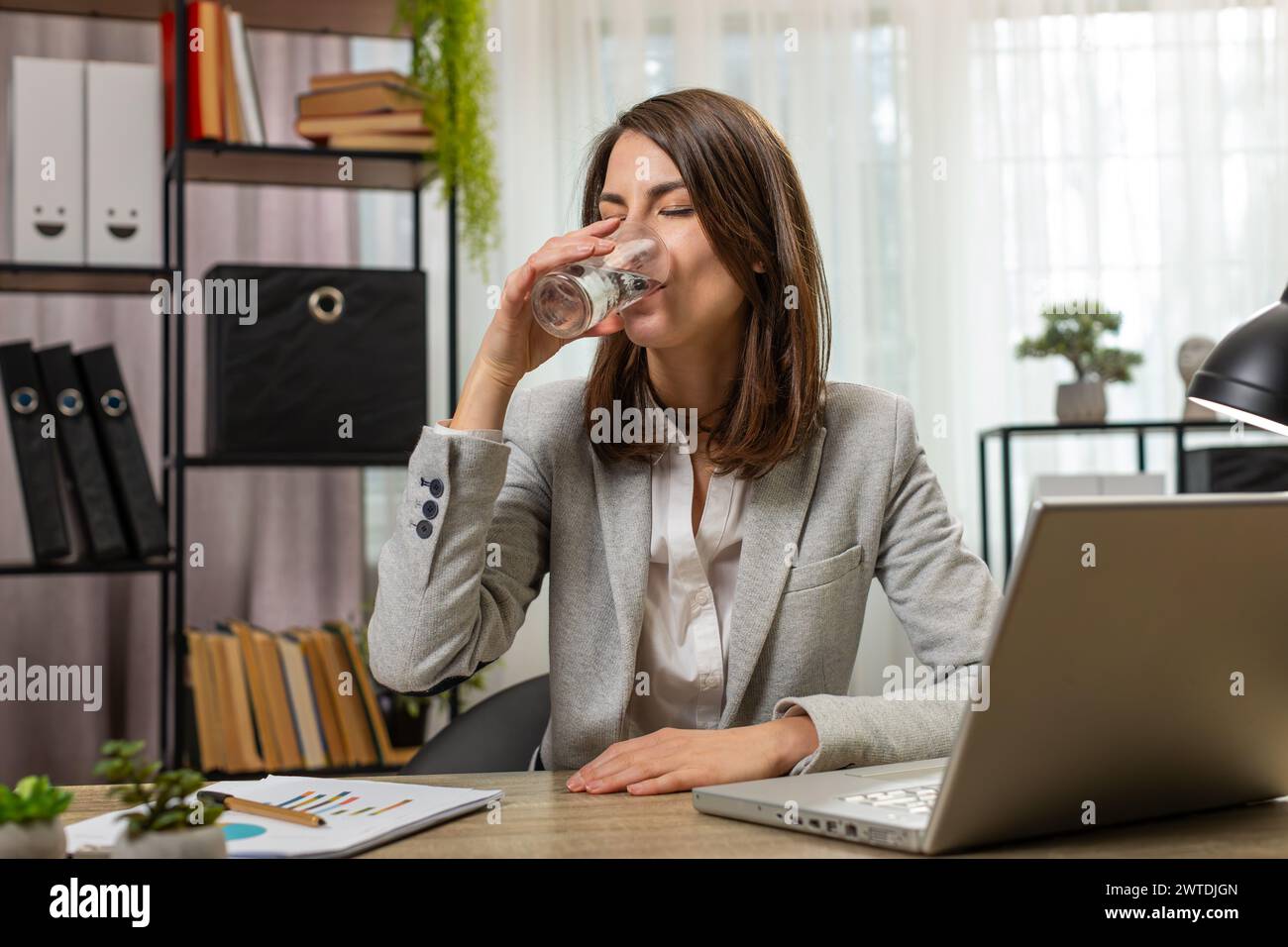 Focused young businesswoman girl sitting at workplace desk drinking ...