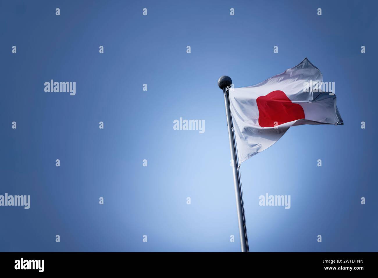 A photograph of a Japanese Rising Sun Flag against a simple blue sky ...