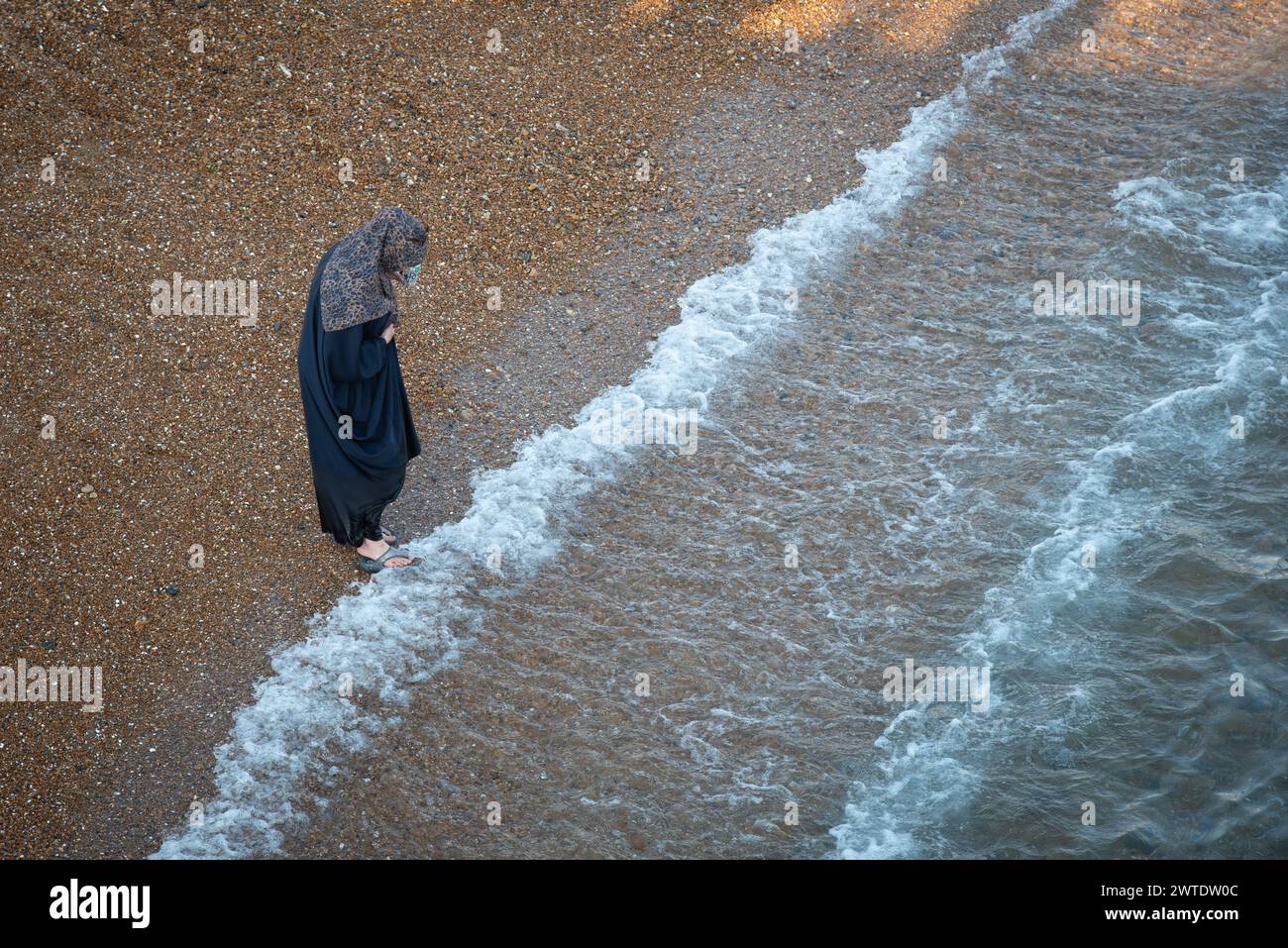 Arabic Muslim woman with traditional black dress walking on the beach ...