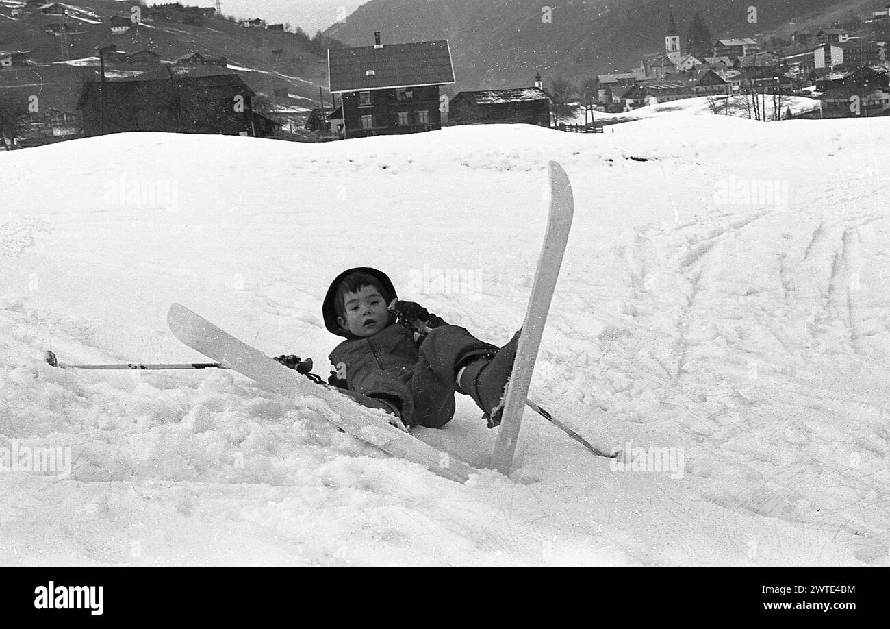 1970s, wintertime and on an alpine mountainside a young boy lying on ...