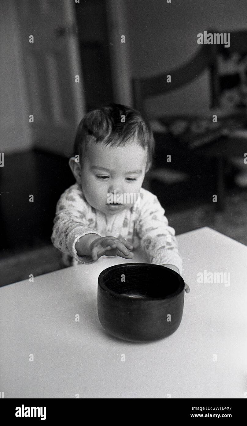 1970s, historical, infant child, little boy, beside a table reaching ...