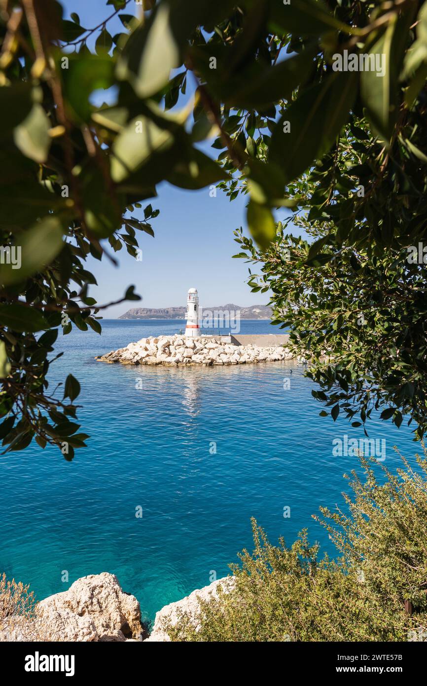 View over white lighthouse through the tree leaves in Kas marina ...