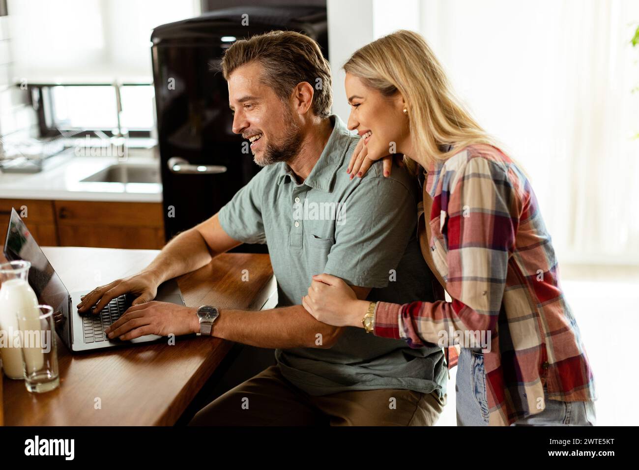 A cheerful couple enjoys a light-hearted moment in their sunny kitchen ...