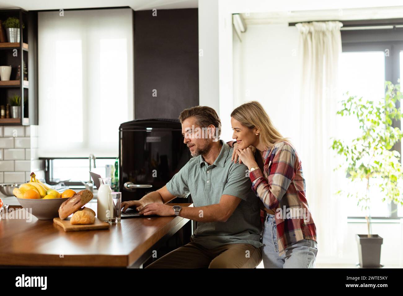 A cheerful couple enjoys a light-hearted moment in their sunny kitchen ...