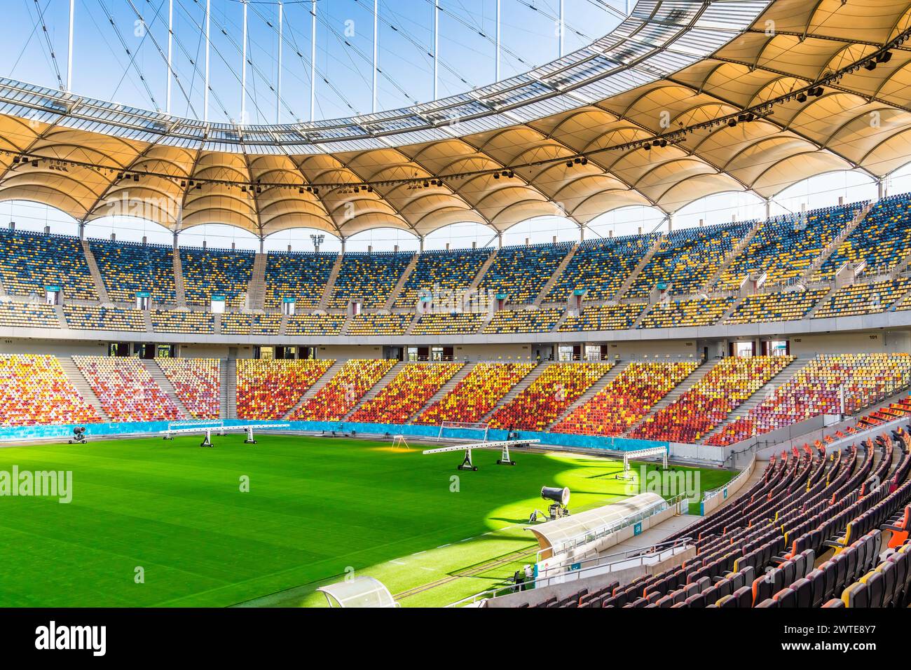 Empty stadium with colored chairs in tribune and the green lawn grass ...