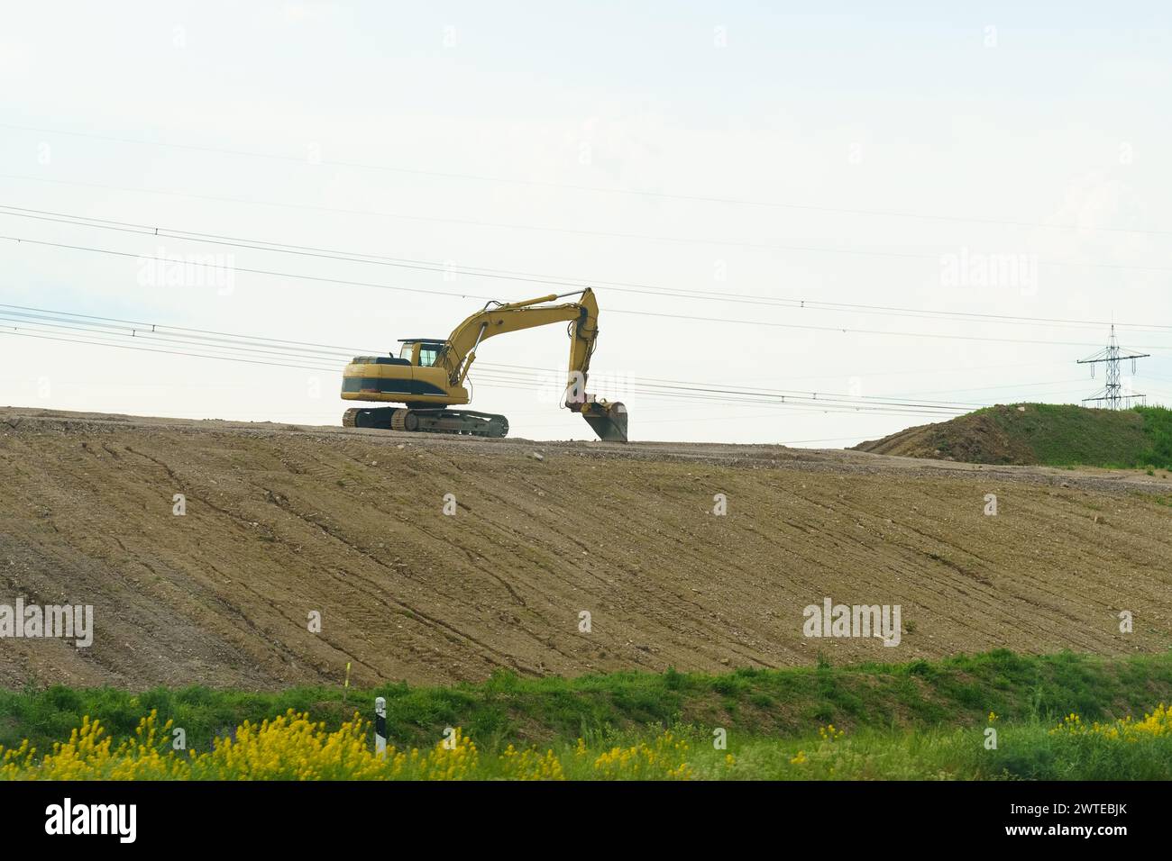 A bulldozer clears a field with power lines in the background ...
