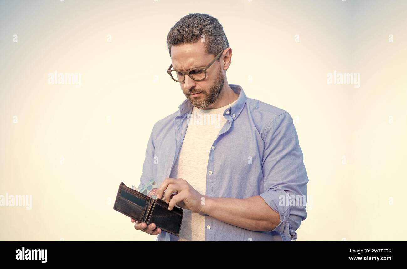 Serious man in glasses taking cash money out of wallet sky background ...